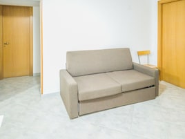 A room with a beige sofa, a wooden door, and a tiled floor.