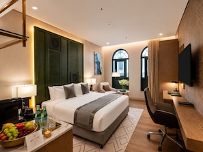 Quarto de hotel com cama grande, escrivaninha, cadeira, televisão e janela com cortinas.