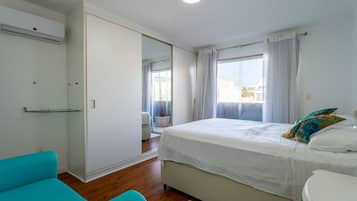 Quarto com cama, guarda-roupa, janela com cortinas e banheiro.