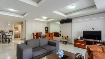 Uma sala moderna com sofá, mesa de centro, televisão e um espaço de jantar com cadeiras e mesa.