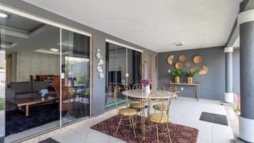 Um espaço de estar moderno com uma porta de vidro que dá para uma varanda, uma mesa de jantar redonda com cadeiras e um sofá ao fundo.