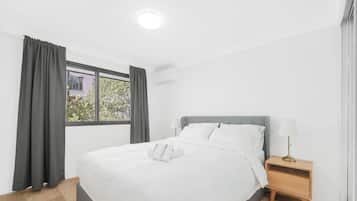 Quarto de hotel moderno e limpo, com uma cama, abajur e janela com cortinas.