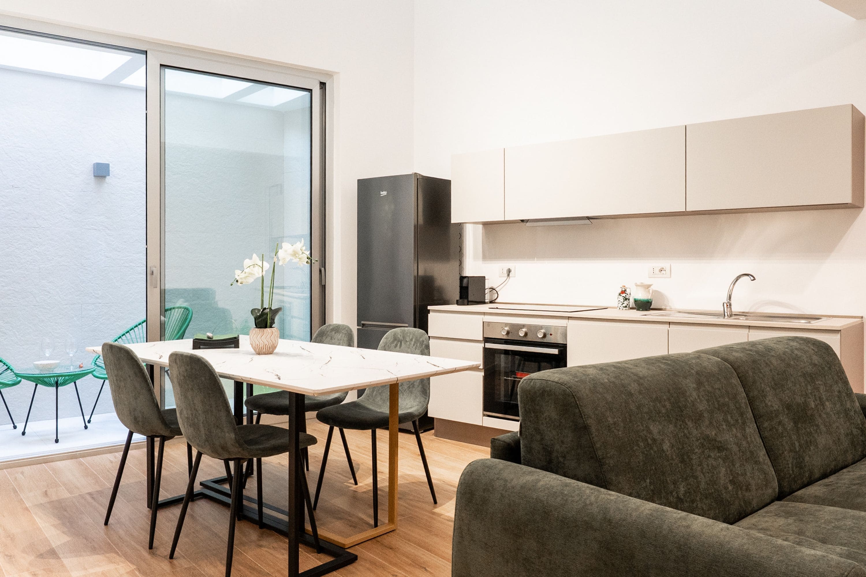 Uma cozinha compacta com área de refeições, um sofá e vista através de uma porta de vidro.