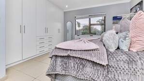 Quarto com um guarda-roupa espaçoso, uma cama com manta texturizada e uma janela com vista para o verde.