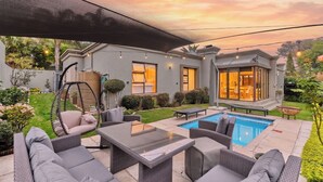 Um quintal com piscina, móveis de jardim e uma área coberta para relaxar.
