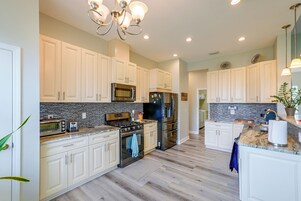 Uma cozinha ampla com armários brancos, eletrodomésticos de aço inoxidável e backsplash em ladrilho em padrão herringbone.