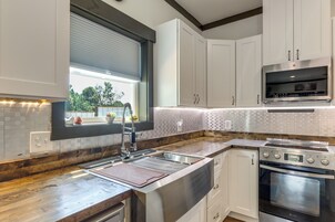 Cozinha moderna com armários brancos, eletrodomésticos de aço inoxidável e janela com vista para o verde.