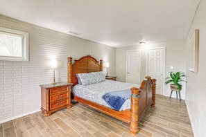 Quarto com cama de madeira, mesa de cabeceira, cômoda e um vaso com planta.