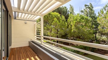 Varanda com piso de madeira e guarda-corpo branco, com vista para um jardim de pinheiros.