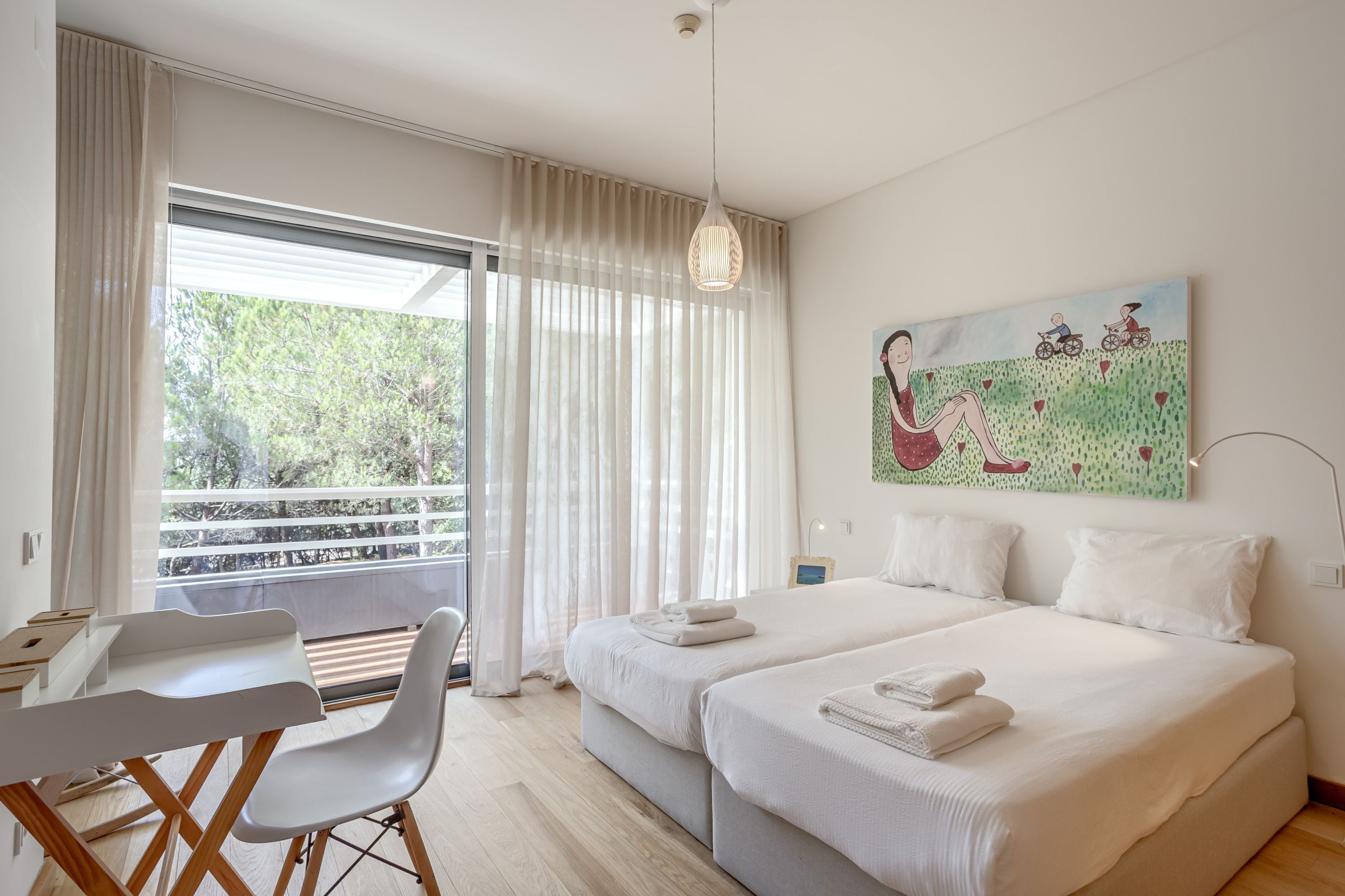 Quarto de hotel com cama, escrivaninha, cadeira e varanda com cortinas.