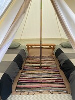 Uma tenda com cama, um banco e um tapete tecido colorido.
