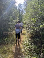 Duas pessoas caminham por uma trilha em meio à floresta, cercadas por vegetação densa.