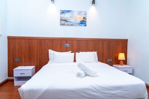 Quarto de hotel com cabeceira de madeira, roupa de cama branca, um quadro na parede e um abajur.