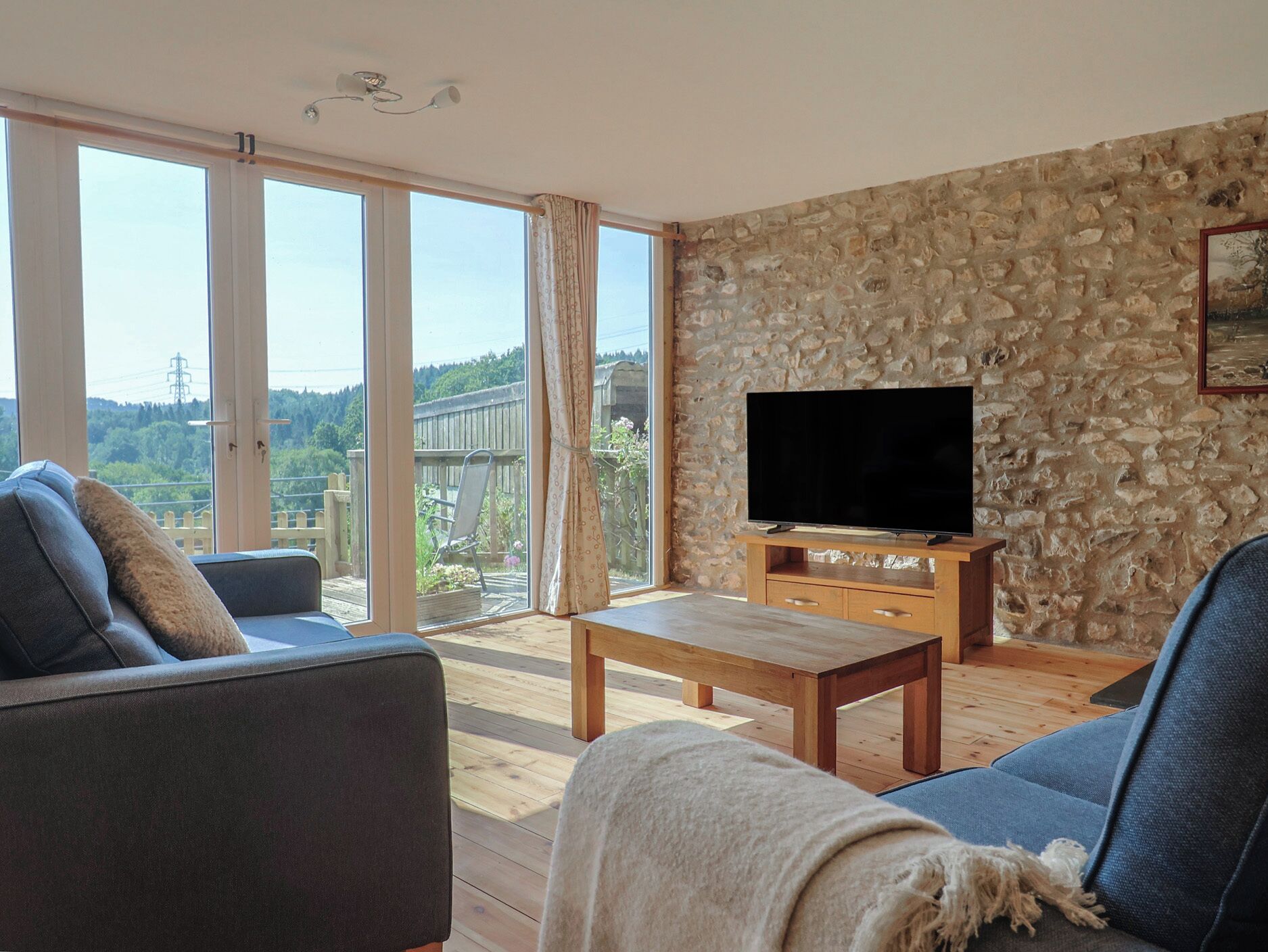 Uma sala de estar com uma parede de pedra, uma televisão de tela plana sobre um suporte de madeira, e uma grande porta de vidro deslizante que dá para um deck.