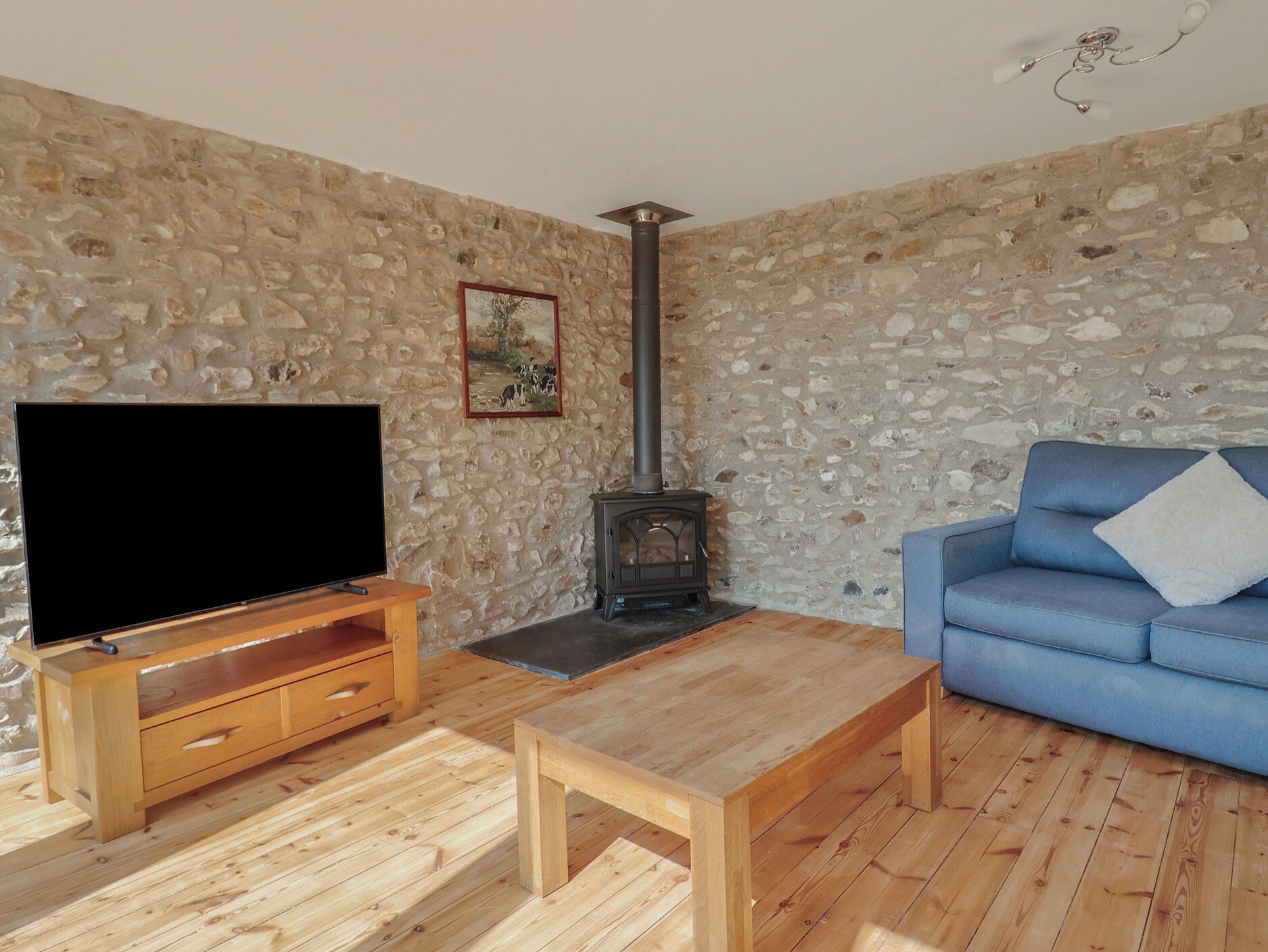 Uma sala de estar com parede de pedra, uma televisão sobre suporte de madeira, um sofá e uma lareira.