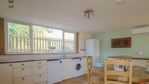 Cozinha compacta com máquina de lavar, mesa de jantar com cadeiras e janela com vista para o verde.