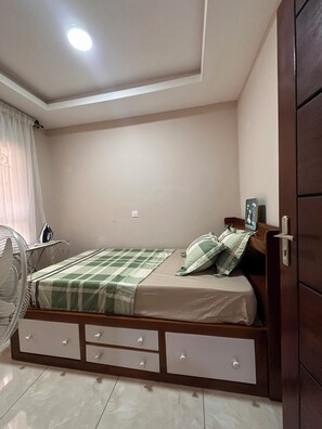Um quarto com uma cama, mesa de cabeceira, ventilador e armário.