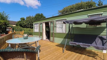 Uma casa móvel com um espaço de pátio que inclui uma mesa, cadeiras, um balanço e uma área de estar coberta.