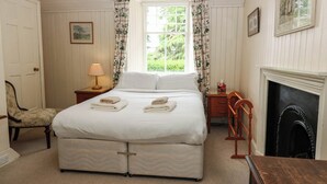 Quarto com cama, cadeira, mesa de cabeceira, lareira e janela com cortinas.