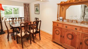 Uma área de jantar com uma mesa e cadeiras de madeira, um penteou com espelho, e uma janela com cortinas.