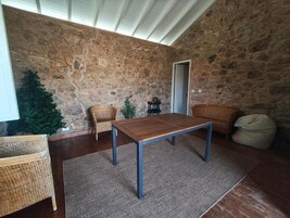 Quarto com parede de pedra, uma mesa de madeira, duas cadeiras de vime, uma pequena árvore de Natal e uma porta.