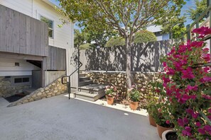 Quintal residencial com muro de pedra, cerca de madeira e plantas em vasos.