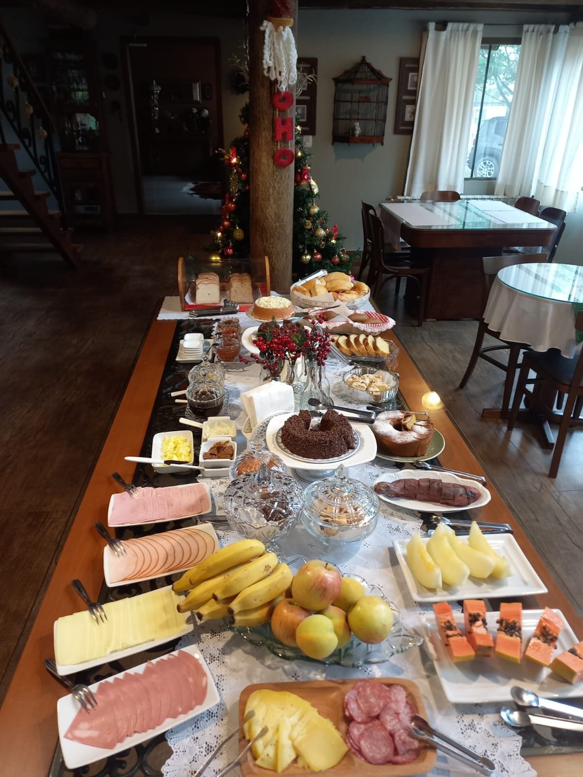Mesa de buffet com diversos alimentos e uma árvore de Natal ao fundo.