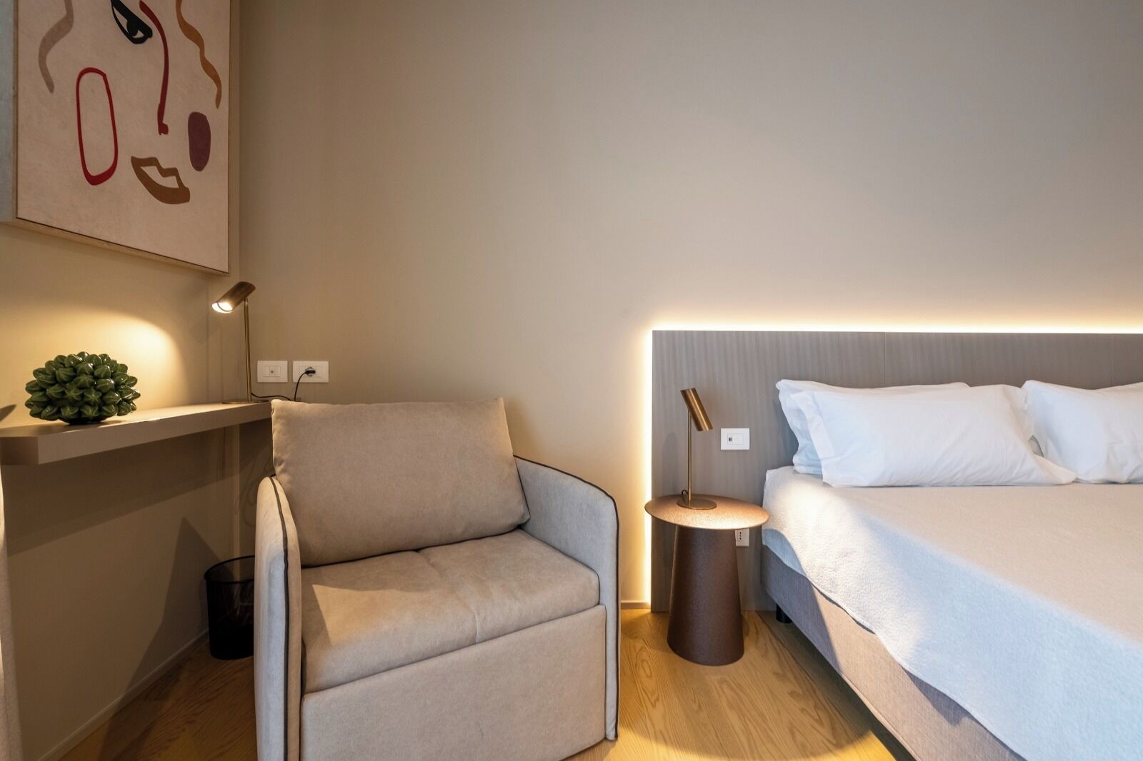 Quarto moderno com sofá, mesa de cabeceira, abajur e cama com roupa de cama branca.