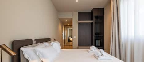 Quarto de hotel com uma cama grande, luminária de cabeceira, armário e vista para o corredor.