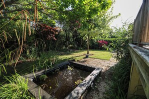Um jardim com lago, cerca de madeira e diversas plantas.