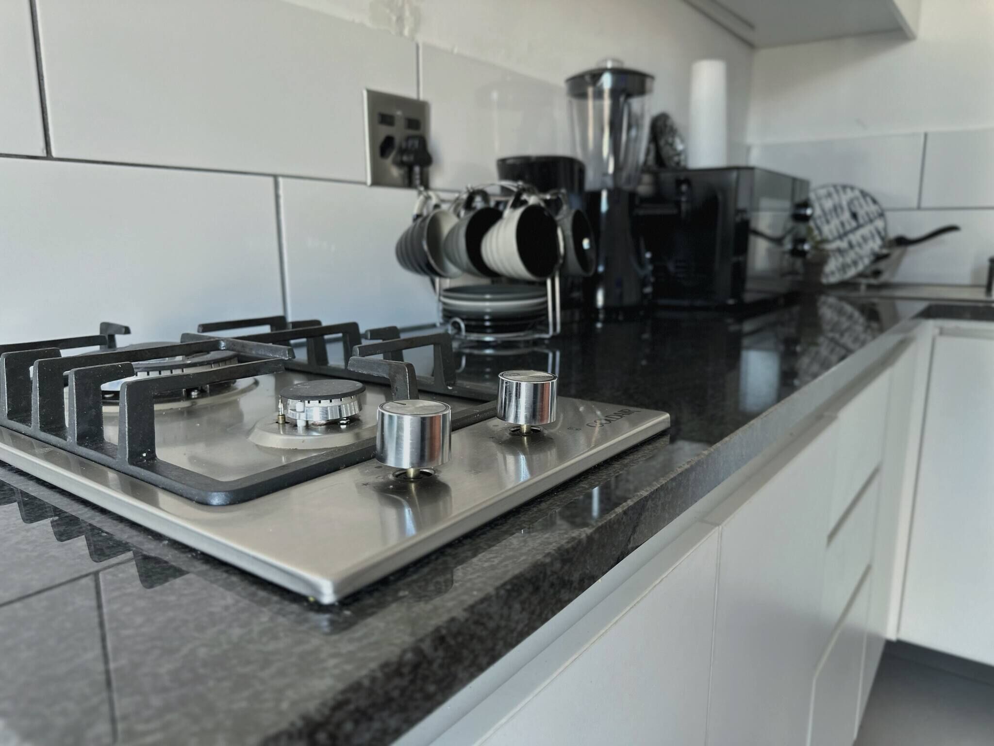 Uma cozinha moderna com fogão a gás, eletrodomésticos de aço inoxidável e armários brancos.