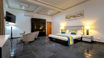 Quarto de hotel moderno com cama, mesas de cabeceira, escrivaninha, cadeira e televisão.