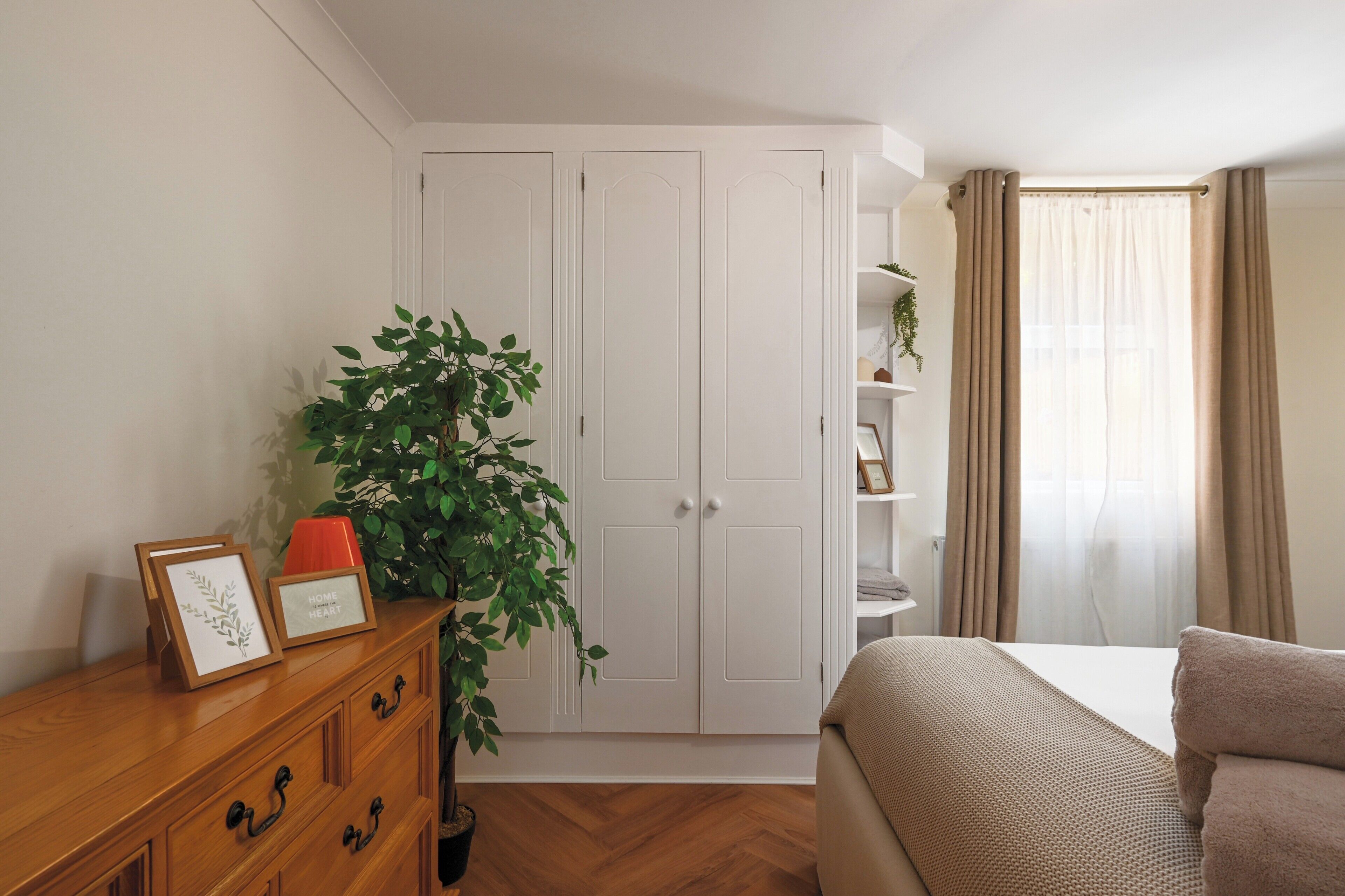 Quarto com cama, penteadeira, planta e guarda-roupa.