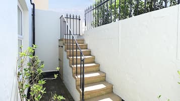 Uma escadaria estreita com corrimão de metal, ladeada por paredes brancas e uma grade de metal preta.