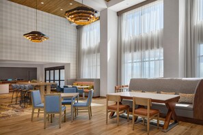 Um hall de hotel espaçoso, com teto alto, mobiliário moderno e grandes janelas que permitem entrada de luz natural.
