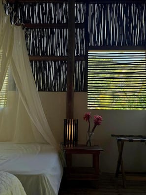 Quarto com uma cama, uma mesinha com flores e uma janela com persianas.