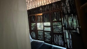 Um quarto com telhado de colmo, uma janela com persianas verticais e um sofá azul.
