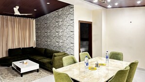 Uma sala de estar moderna com uma mesa de centro branca, sofá verde e uma mesa de jantar de mármore com quatro cadeiras.