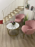 Uma escadaria com corrimão, uma mesa redonda de mármore com um arranjo de flores e duas cadeiras cor-de-rosa.