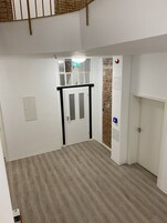 Quarto com piso de madeira, paredes brancas, porta com painéis de vidro fosco, parede de destaque em tijolos e luminária no teto.