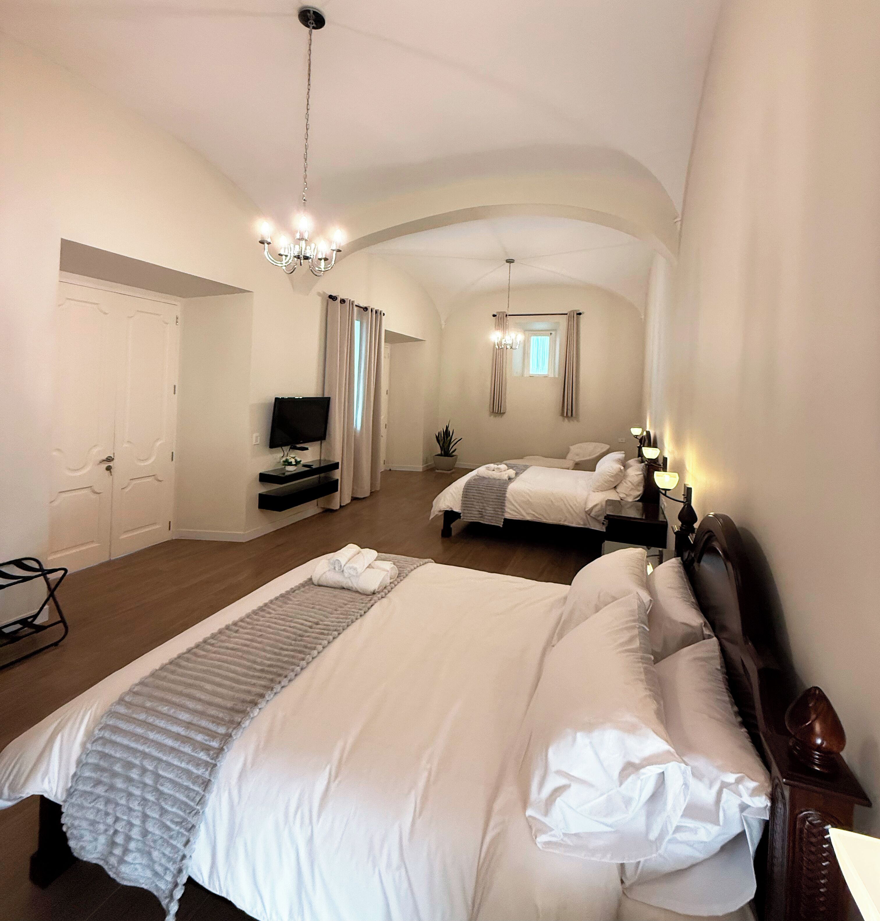 Um quarto espaçoso com duas camas, uma televisão e um candelabro.