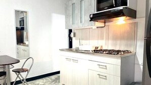 Uma cozinha compacta com fogão a gás, micro-ondas e lixeira.