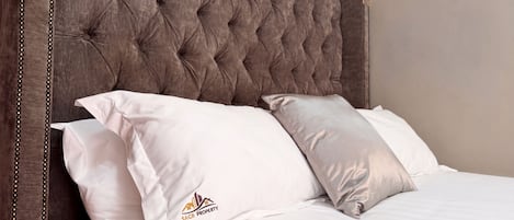 Cama com cabeceira acolchoada, duas almofadas e um logotipo em uma delas.