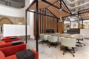 Uma sala de conferência moderna com uma mesa comprida, várias cadeiras e uma área de estar vermelha.