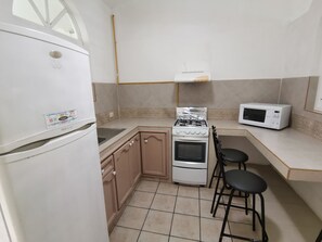 Uma cozinha compacta com geladeira, fogão, micro-ondas e dois bancos altos.