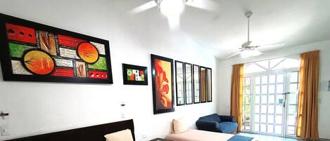 Quarto de hotel com duas camas, ventoinha no teto e uma janela grande com cortinas.