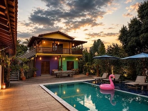 Uma área de piscina com deck de madeira, um flutuador de flamingo rosa e um edifício com varanda.