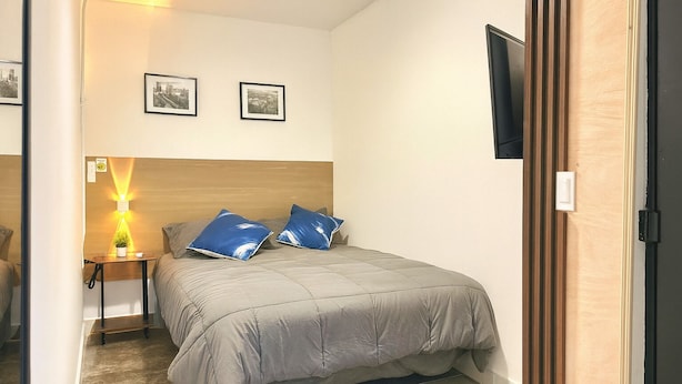 Um quarto com cama, almofadas, mesa de cabeceira, abajur e duas fotos emolduradas na parede.