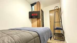 Quarto com cama, TV fixada na parede e escada encostada.
