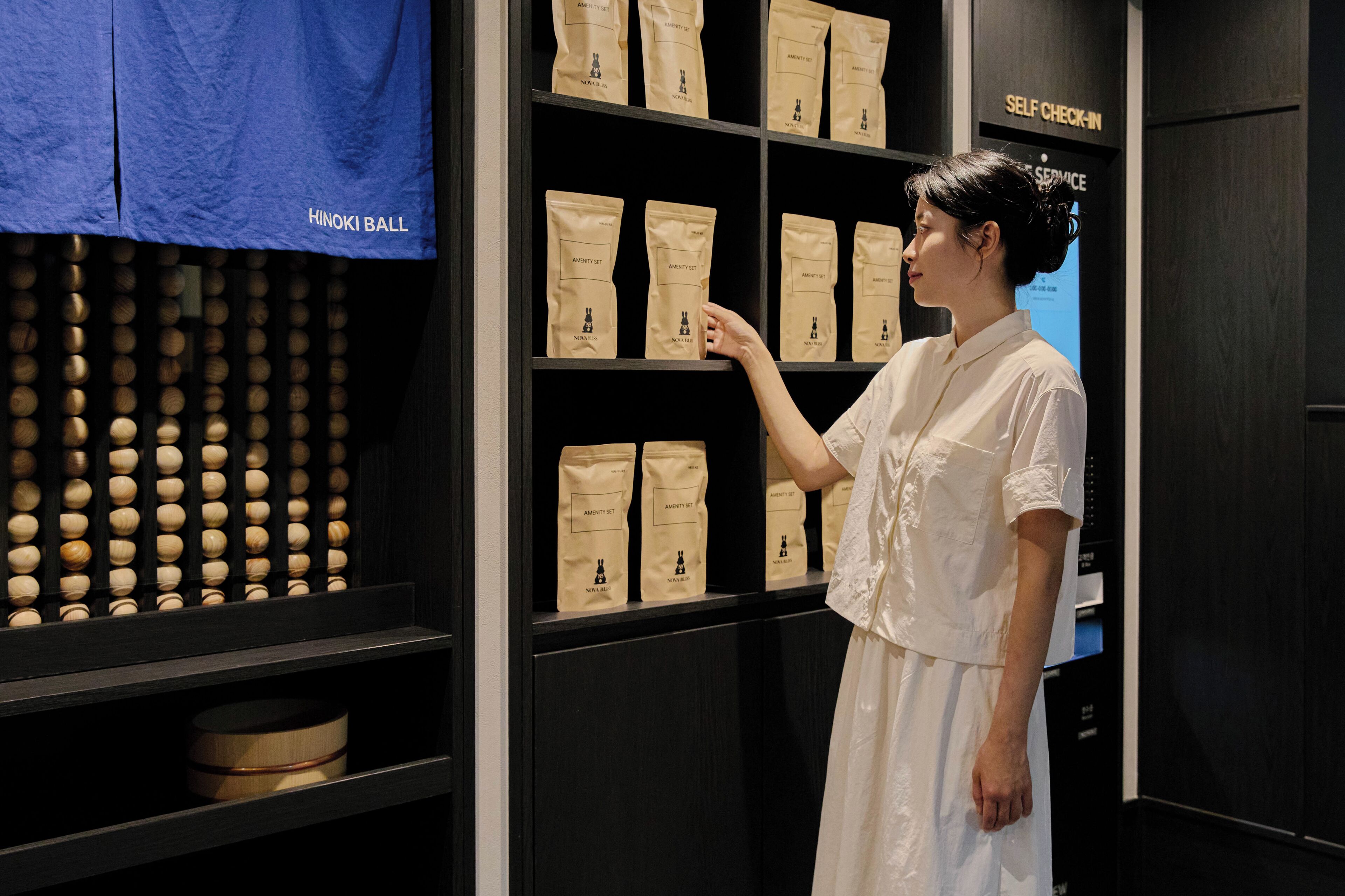 A woman in a white dress examining packaged items on shelves in a store with a blue cloth and wooden balls in the background.